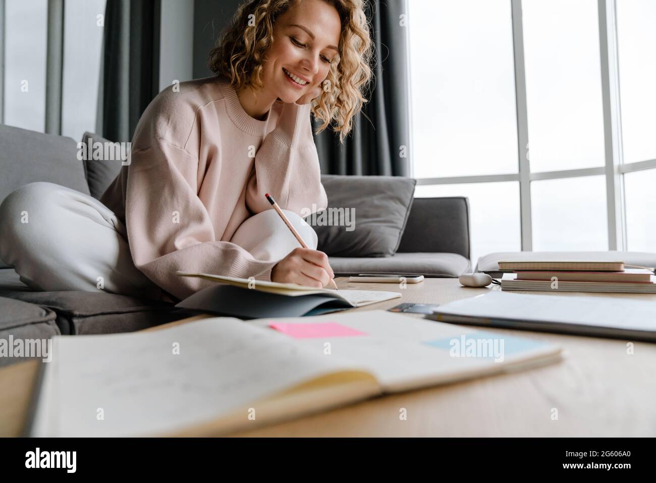 Young white woman smiling and writing down notes while sitting on couch ...