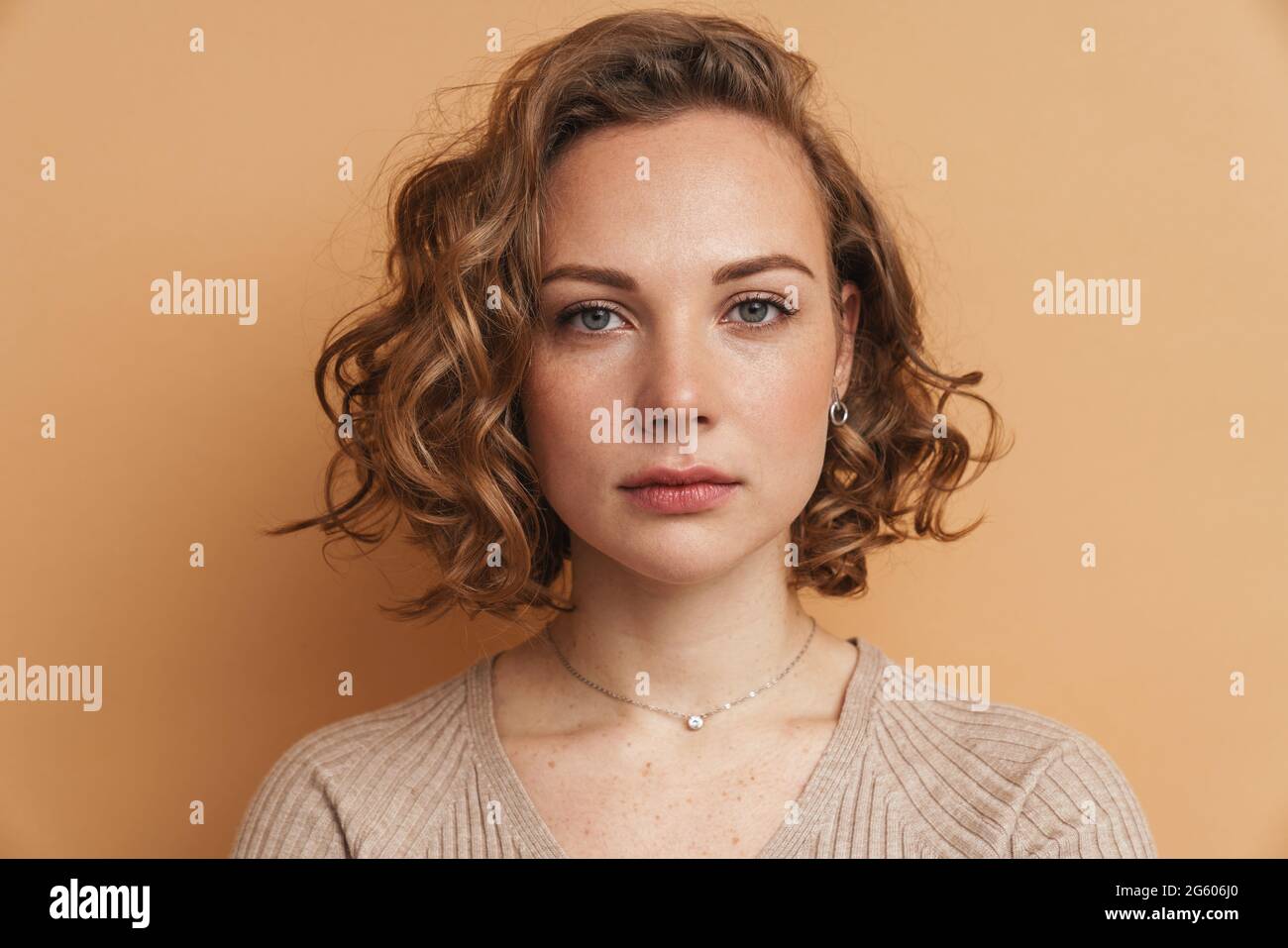 Young ginger woman with wavy hair posing and looking at camera isolated ...