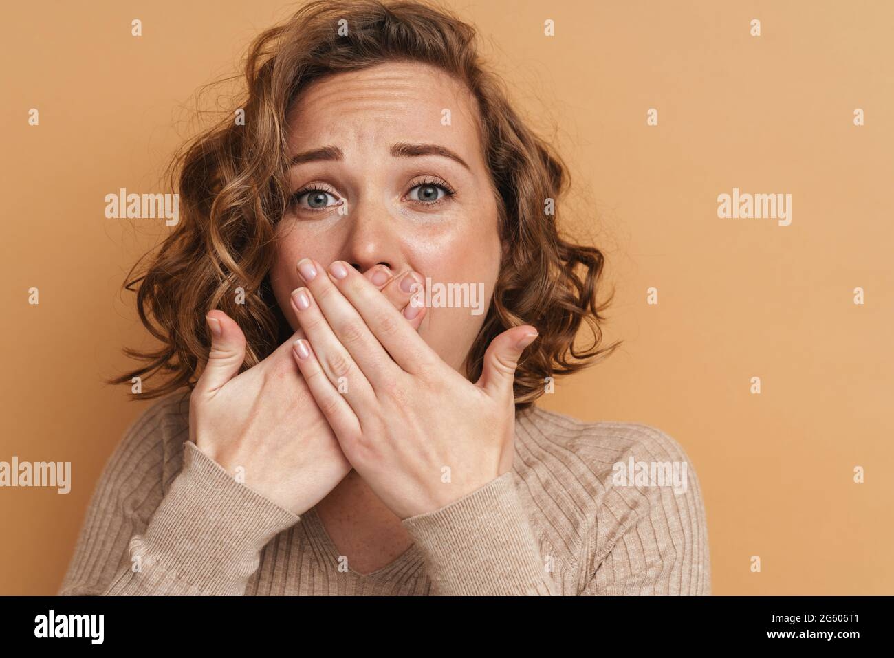 Young ginger scared woman with wavy hair covering her mouth isolated ...