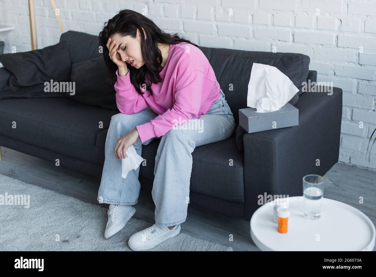 diseased young woman sitting on couch with hand near face and holding ...