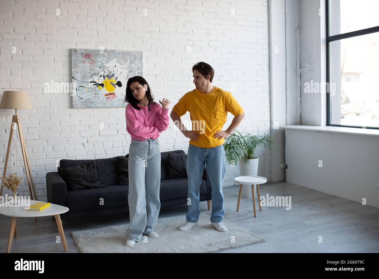 angry young man standing in hands on hips pose near girlfriend with ...