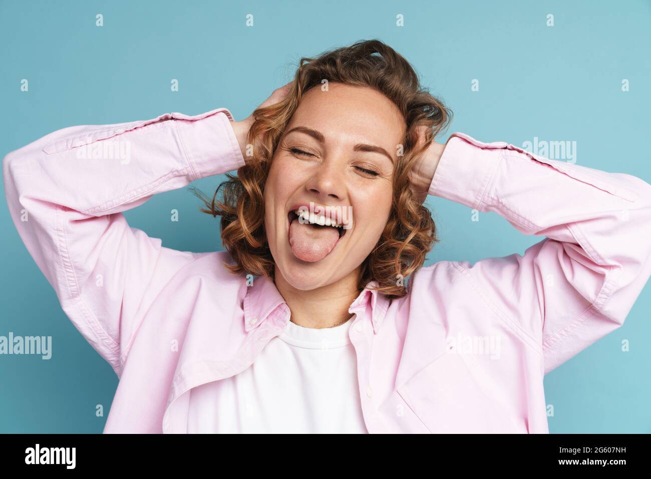Young ginger woman showing her tongue while holding her head isolated ...