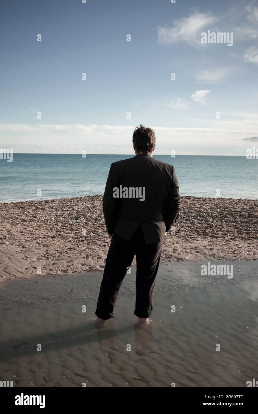 rear view of tall man with dark hair in dark suit with his hands in ...