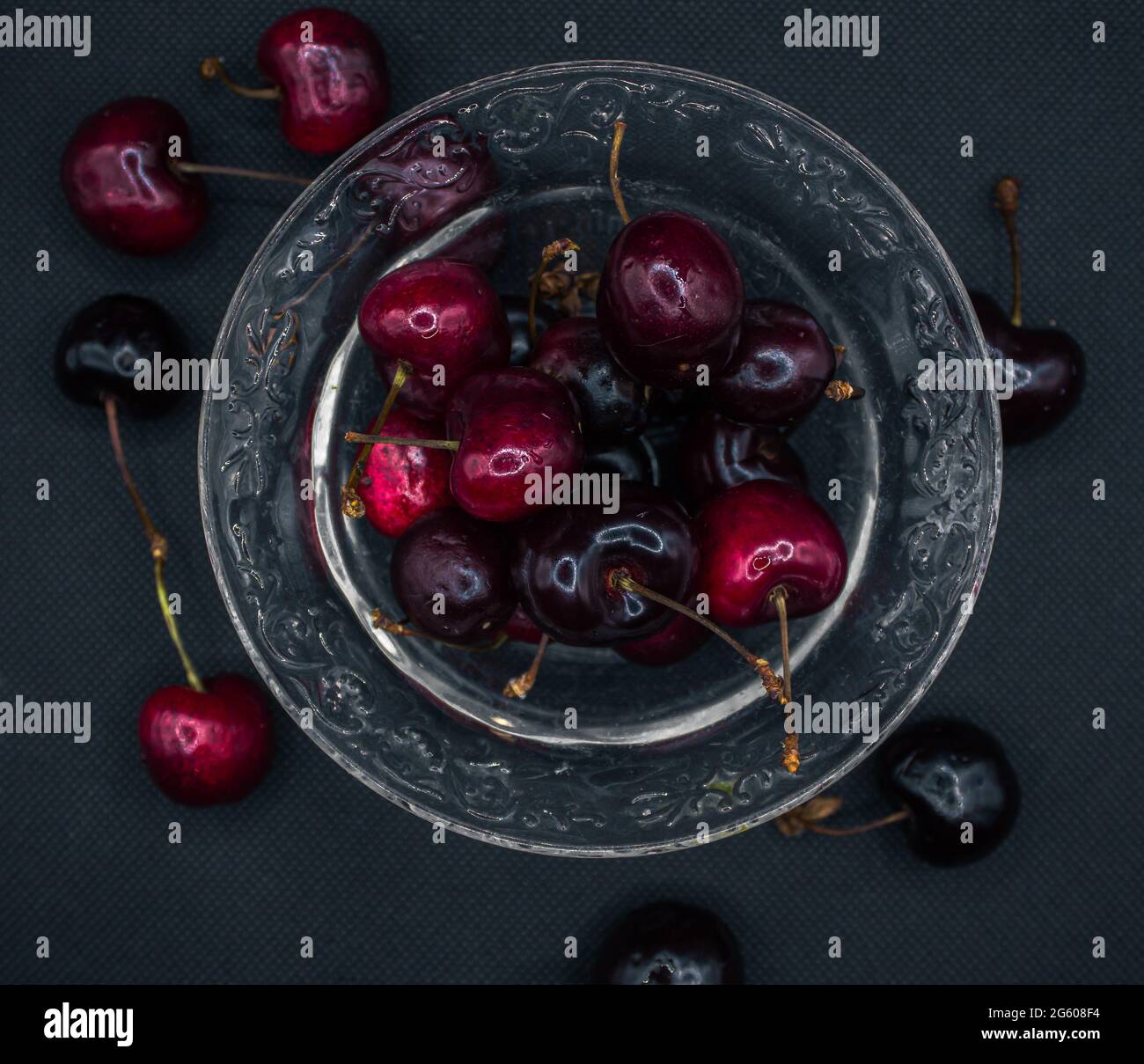 Cherries with water drops in a transparent glass jar on a black table ...