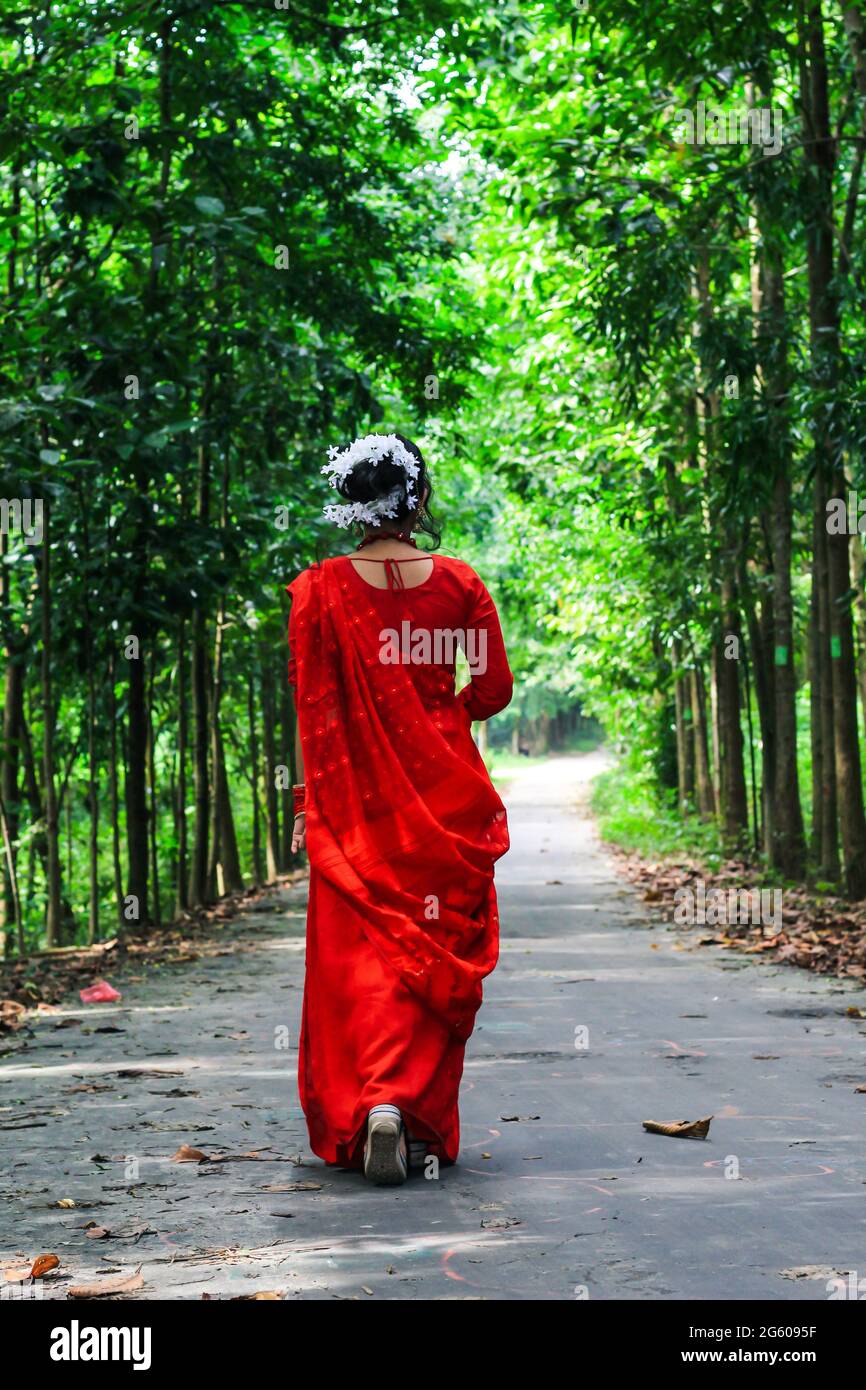 Young woman wearing a red saree walking on green asphalt road. The girl ...
