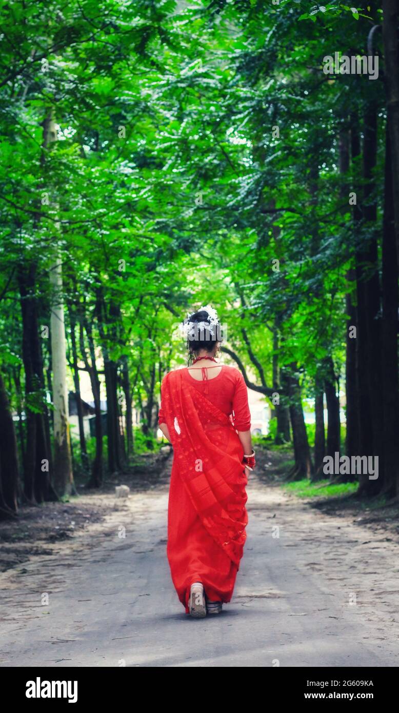 Young woman wearing a red saree walking on green asphalt road. The girl ...