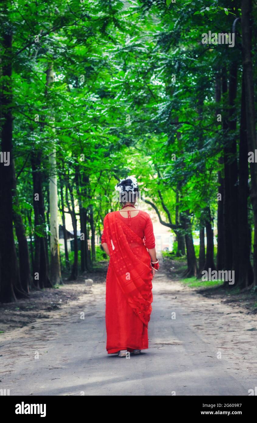 Young woman wearing a red saree walking on green asphalt road. The girl ...
