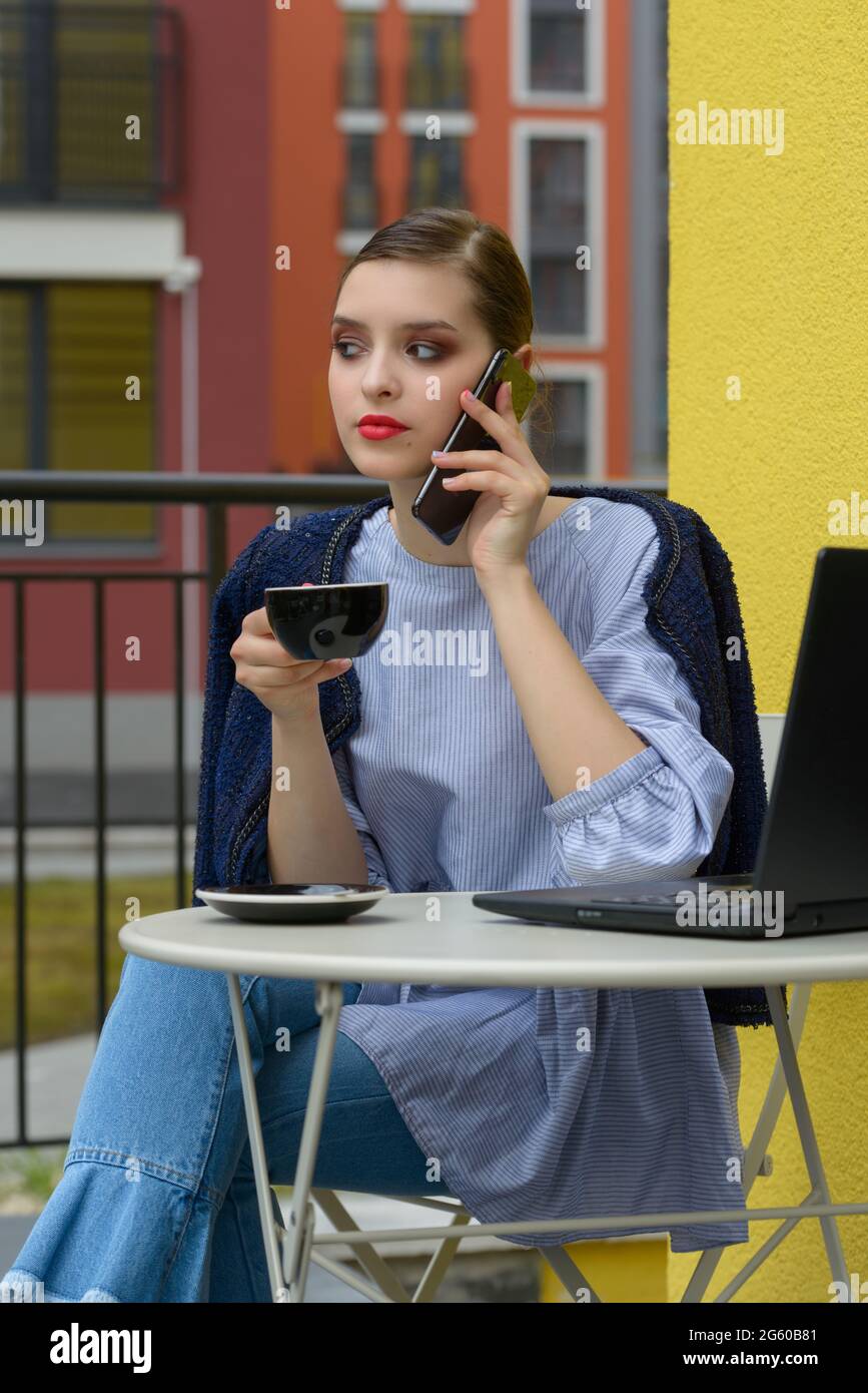 Charming happy woman student communicates by phone and use laptop ...
