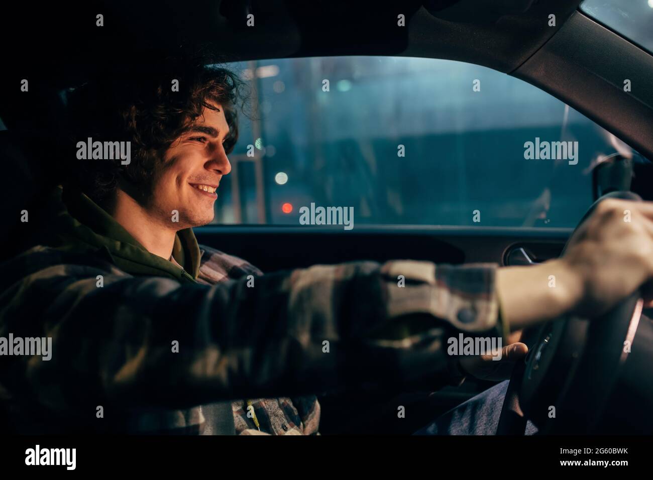 Side view of cheerful driver sitting in car in evening Stock Photo - Alamy
