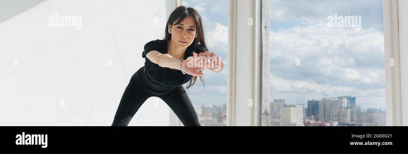 slim armenian woman doing forward bend exercise near window and white ...