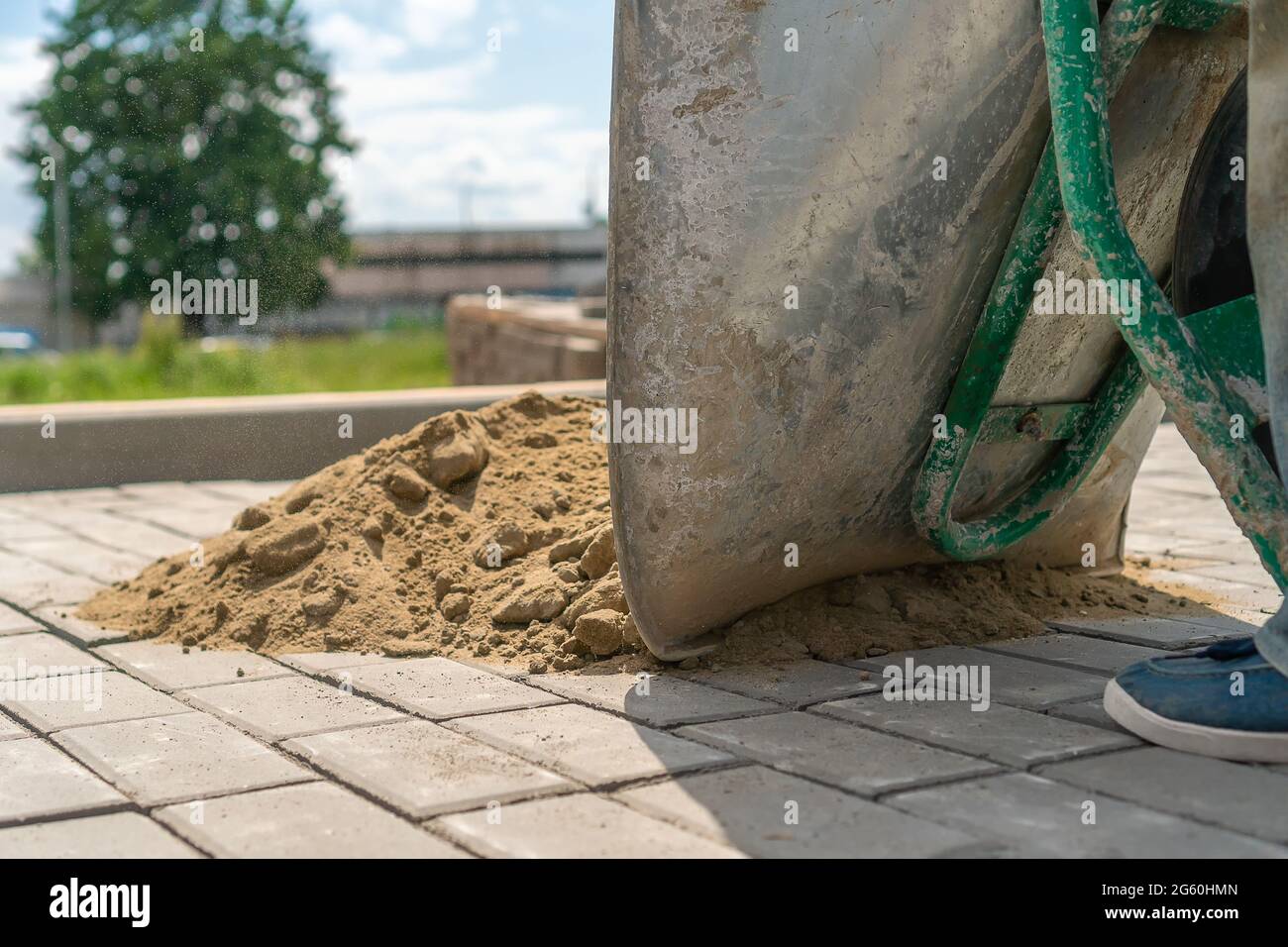 Close-up of a man from a construction wheelbarrow pouring sand on a new ...
