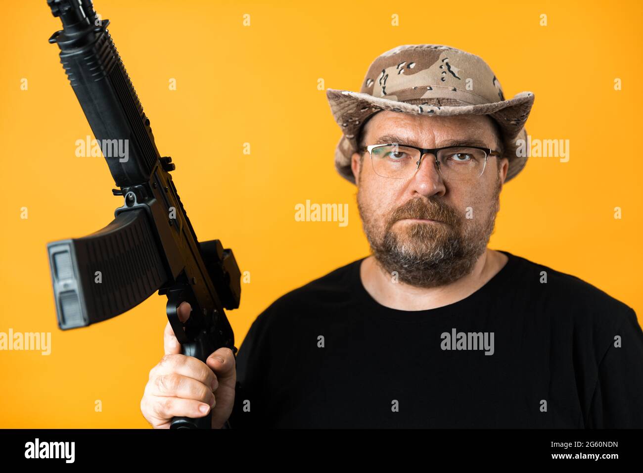 Middle aged man with rifle in black t-shirt and hat against yellow ...