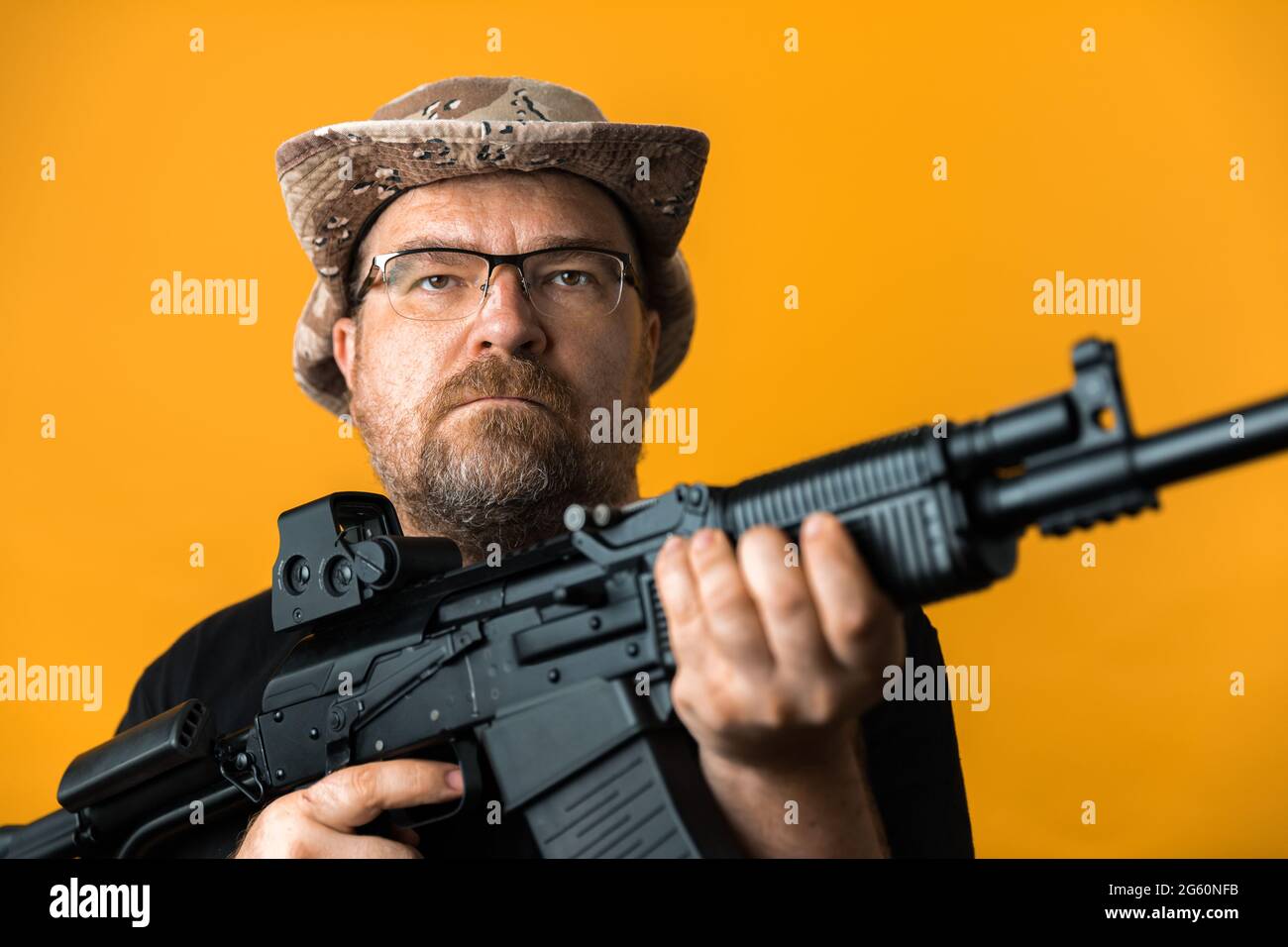 Middle aged man with rifle in black t-shirt and hat against yellow ...