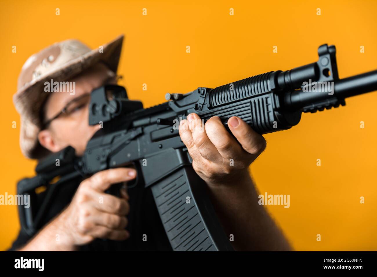 Middle aged man with rifle in black t-shirt and hat against yellow ...