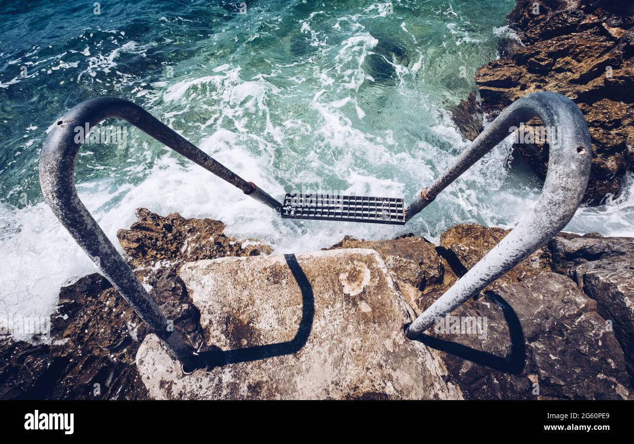 Wide angle shot of a metal ladder on the rocky shore beach washed by ...