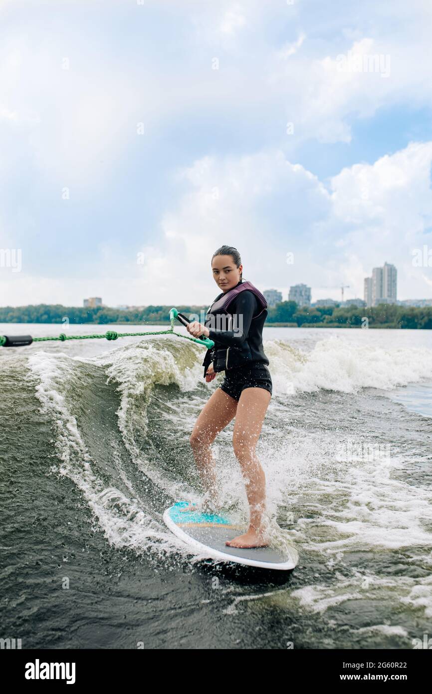 Young woman wakesurfing on river is towed behind a motorboat by wire ...