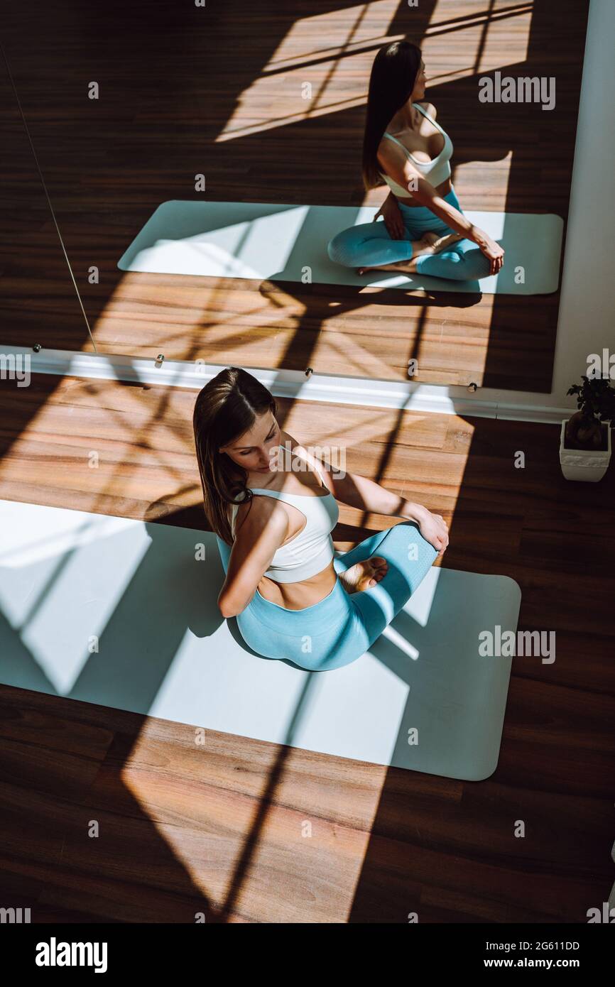 Young fit woman do stretching exercises in front of a mirror on a mat ...