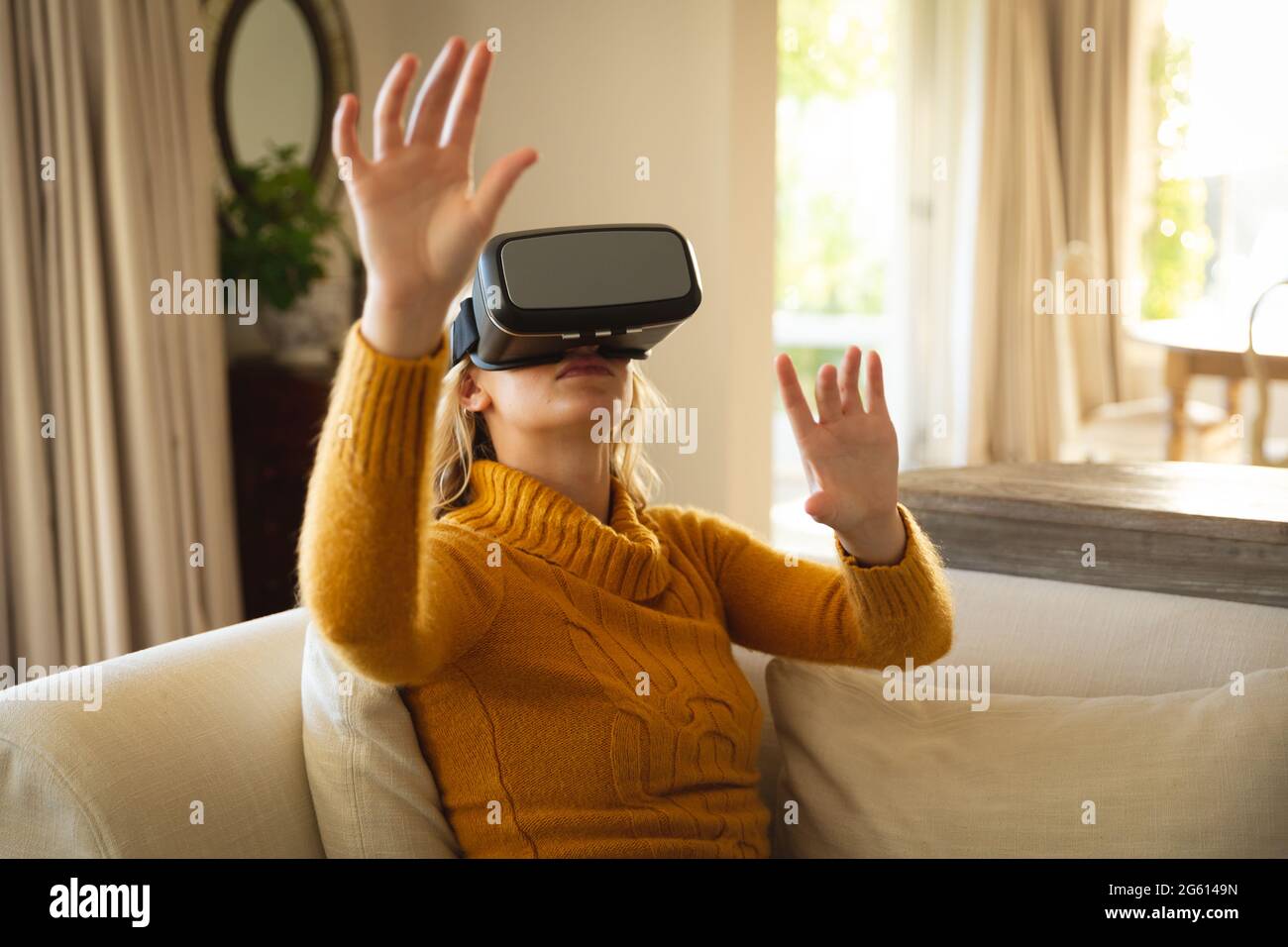 Caucasian woman sitting on couch in luxury living room wearing vr ...