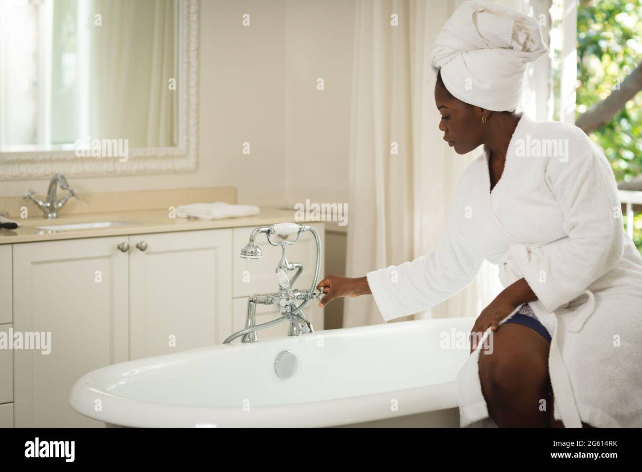 African american woman sitting in bathroom wearing bathrobe and towel ...