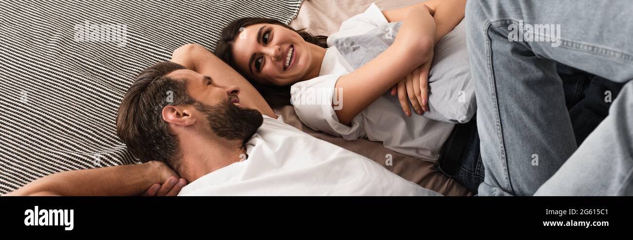 Happy woman with pillow looking at boyfriend on bed, banner Stock Photo ...