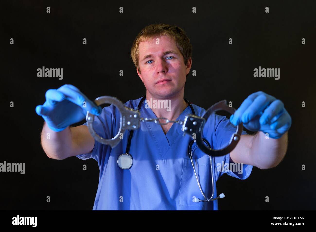 Sad paramedic in blue uniform holding handcuffs on dark background ...