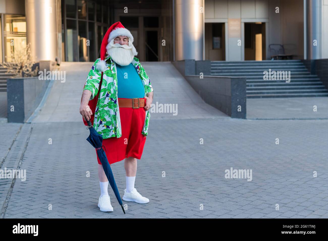 Santa Claus dressed in shorts walks around the city with an umbrella ...