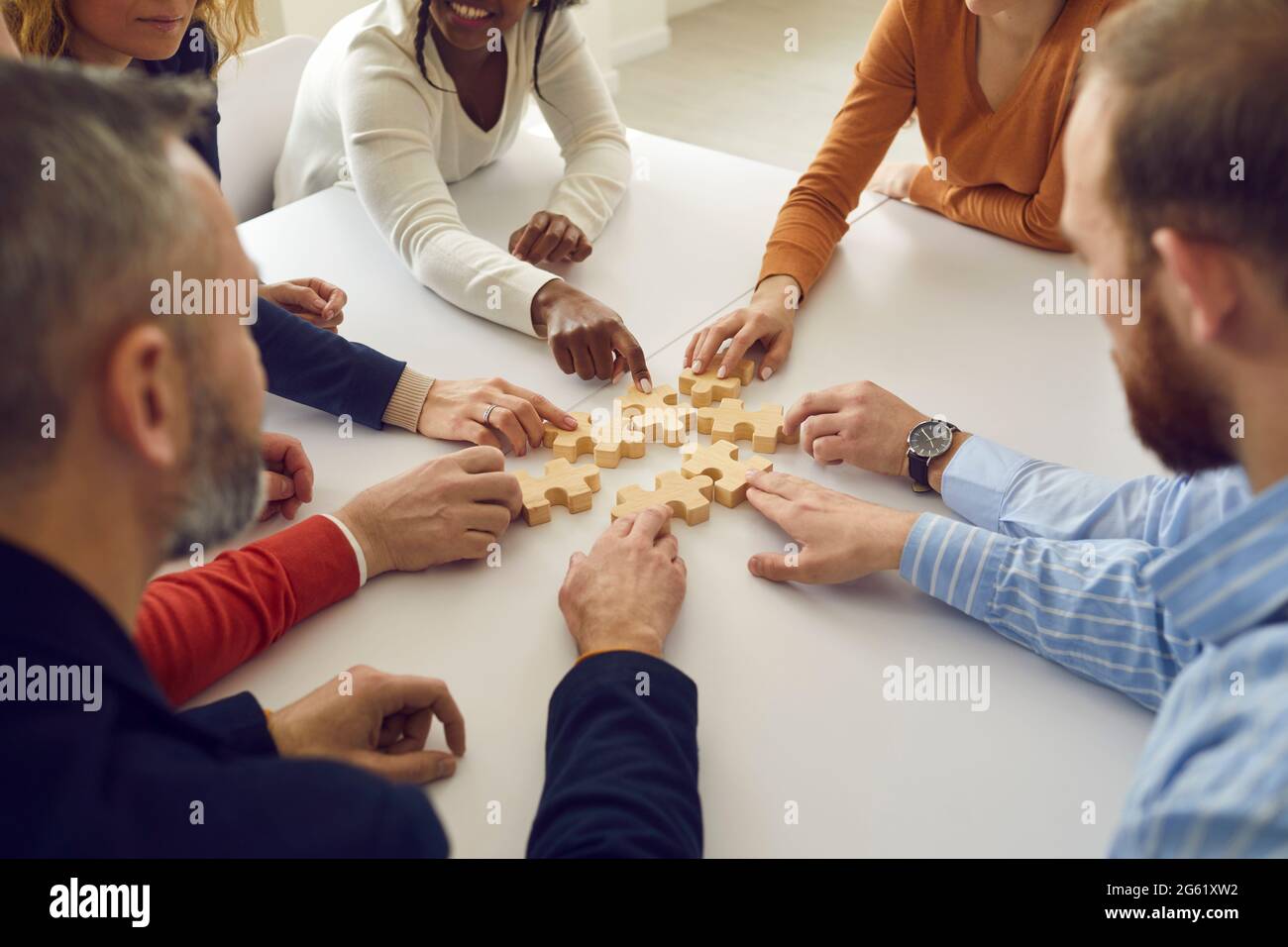 Diverse team of business people sitting around table and joining jigsaw ...