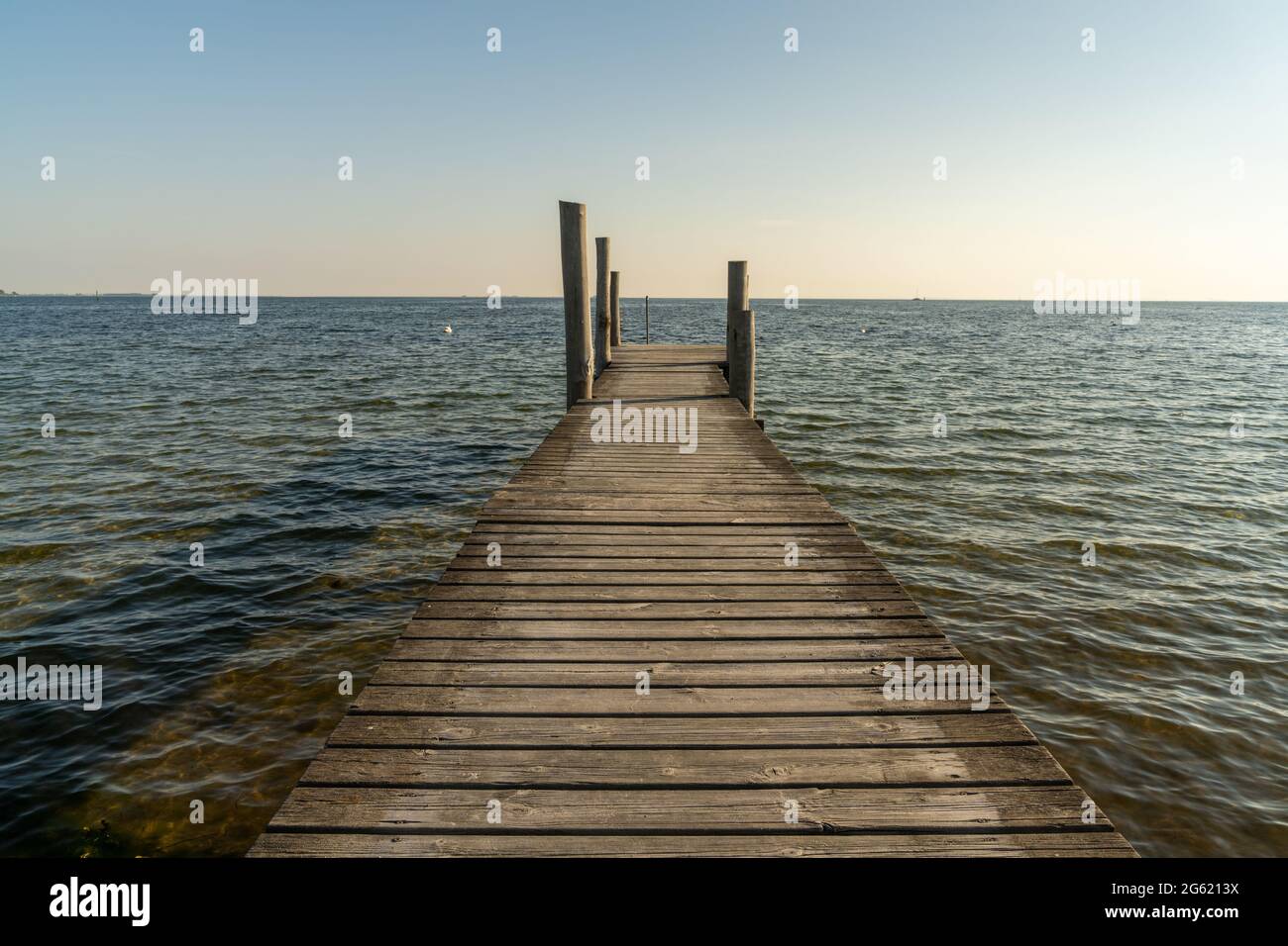 A wooden dock leading out into a calm blue ocean in evening light Stock ...