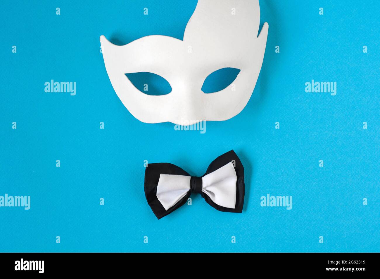 A black and white bow tie and a white carnival mask on a pastel blue ...