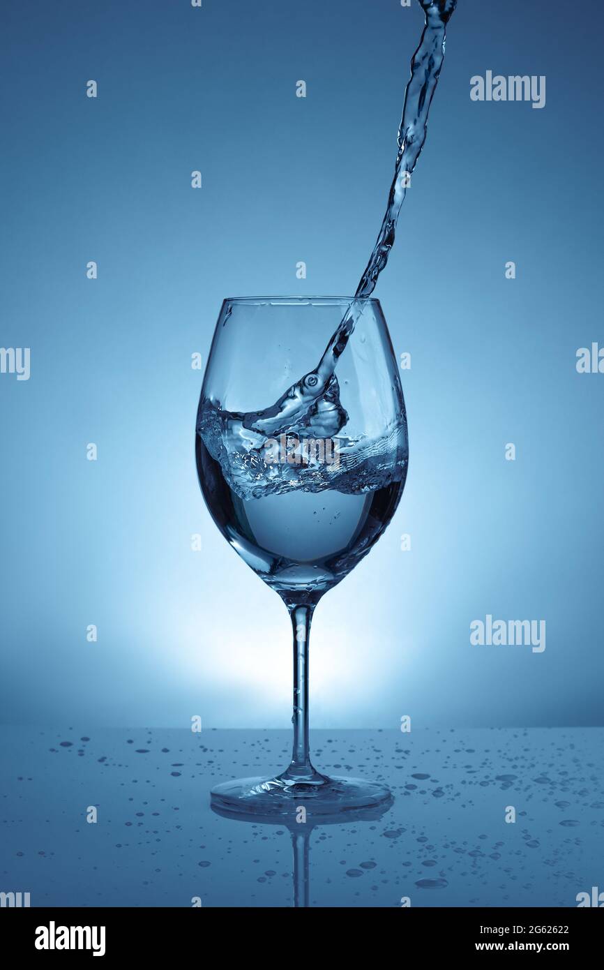 pouring water into a transparent glass for wine. light blue background ...