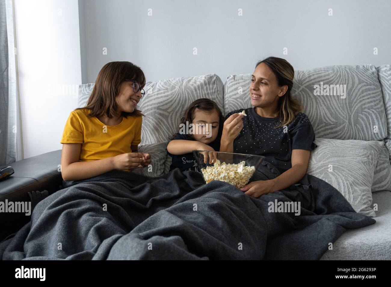 Caucasian mother and daughters, sitting on the living room couch ...