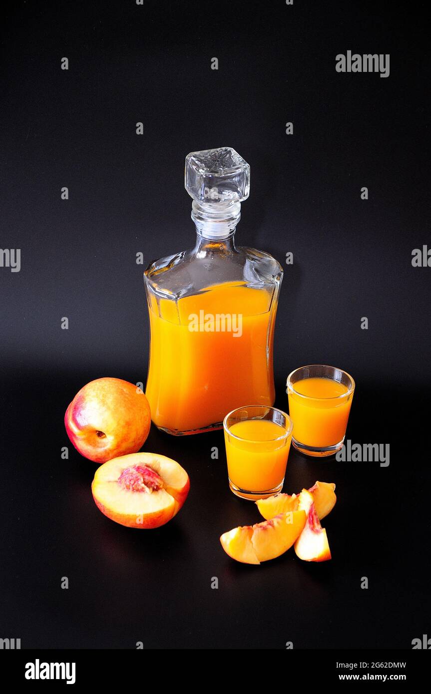 Homemade apricot liqueur in two glasses and a glass decanter, next to pieces of ripe fruit on a ...