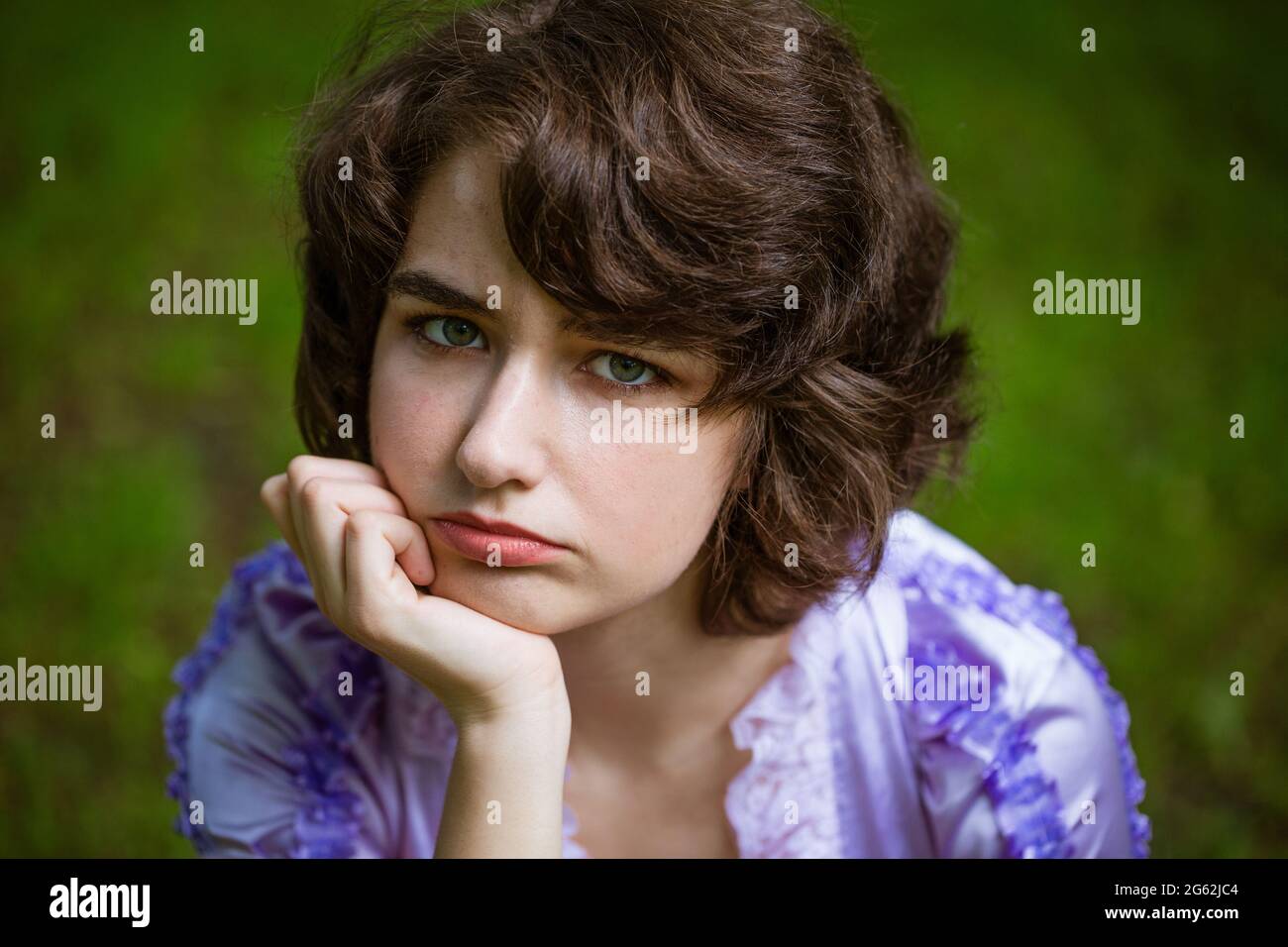 Rubs young sad woman on natural background. Cute girl looks into the ...
