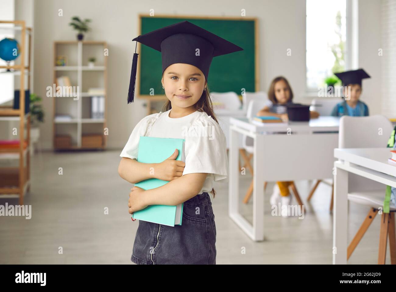 Portrait of a cute little elementary school graduate girl who is ...