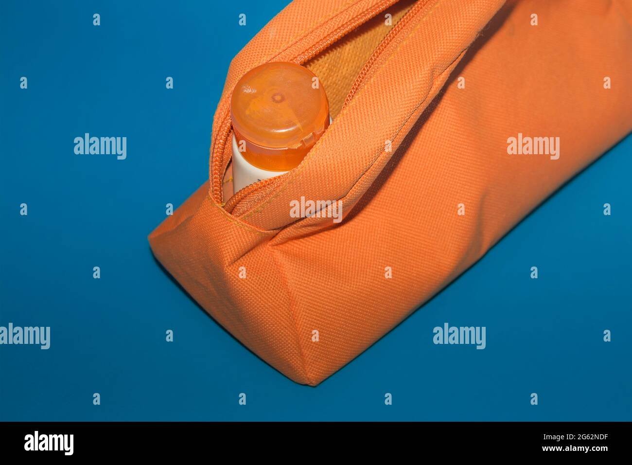 Orange cosmetic bag with a orange cap of sunscreen on a blue background ...