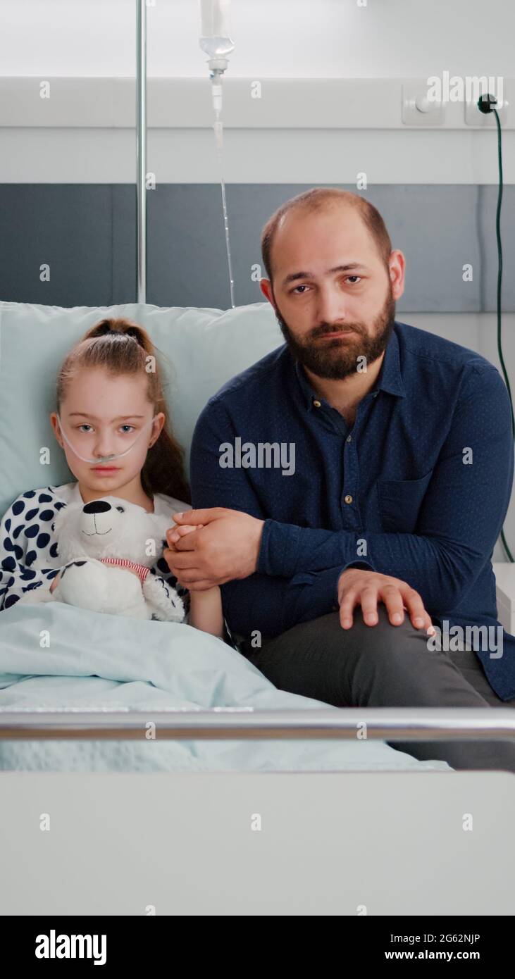 Portrait of sad father holding sick child hands looking into camera ...