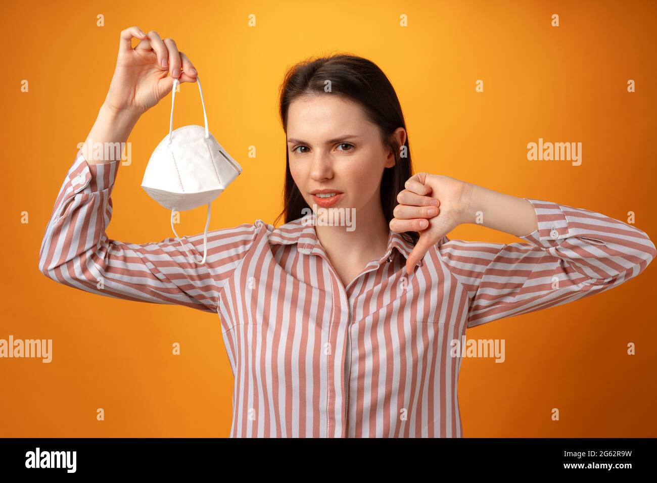 Studio portrait of a young woman taking off her face mask against ...
