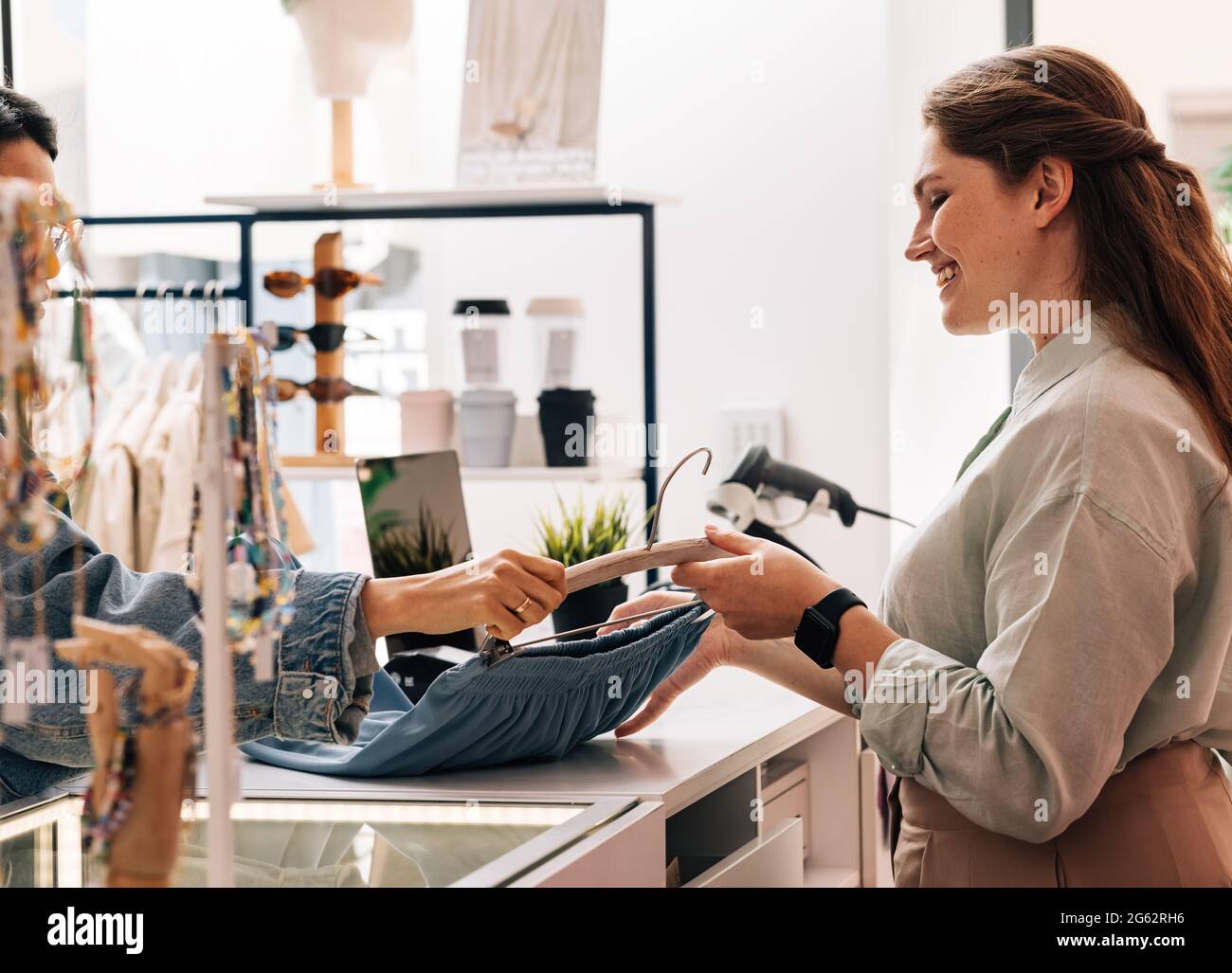 Side view of saleswoman helping buyer with clothes at fashion store ...