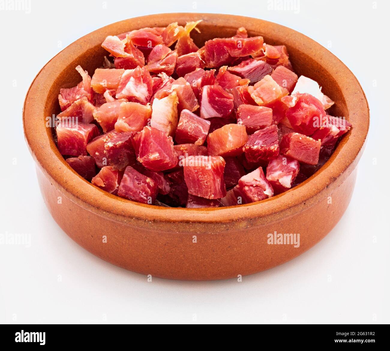 Iberian ham (serrano) cut into cubes (diced). In clay bowl. Isolated on ...