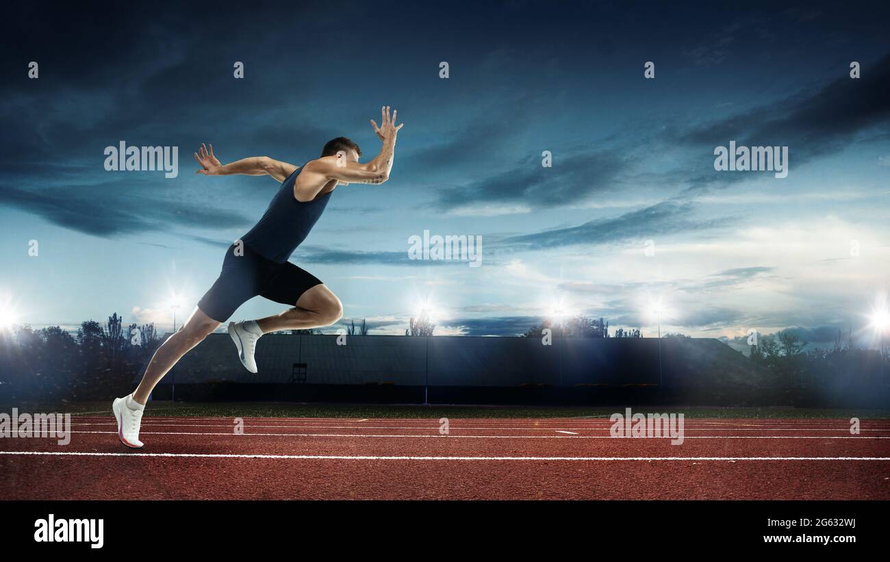 One professional male runner, jogger training at stadium in evening ...