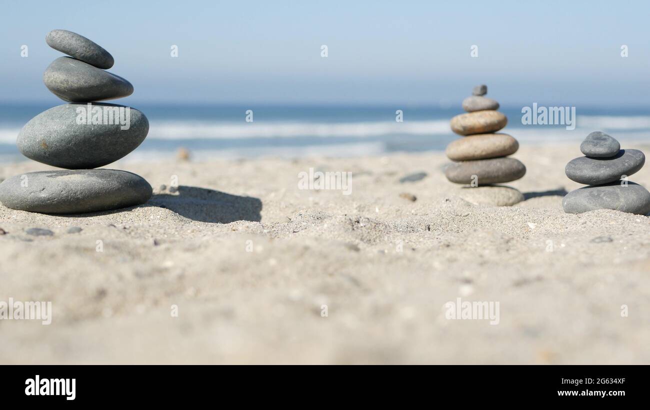 Rock balancing on ocean beach, stones stacking by sea water waves ...