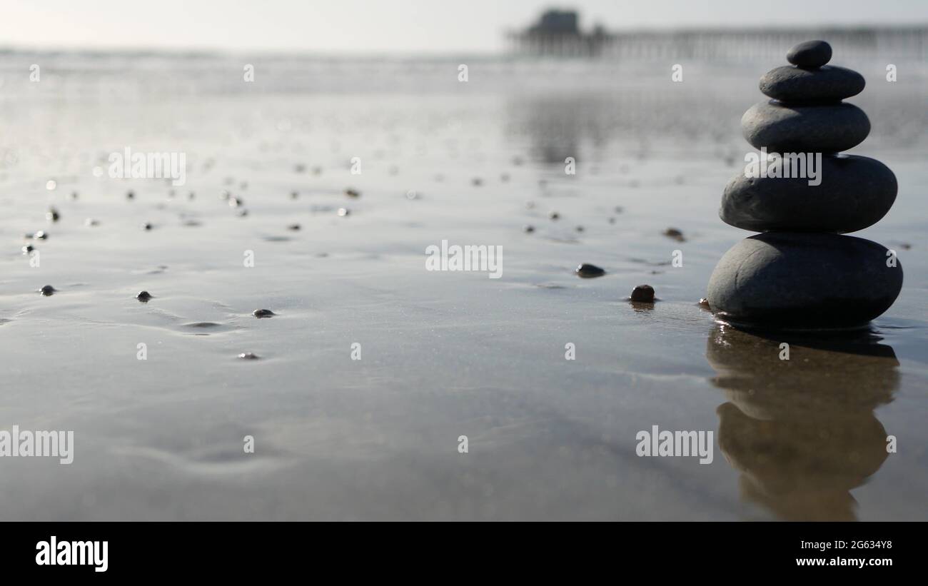 Rock balancing on ocean beach, stones stacking by sea water waves ...