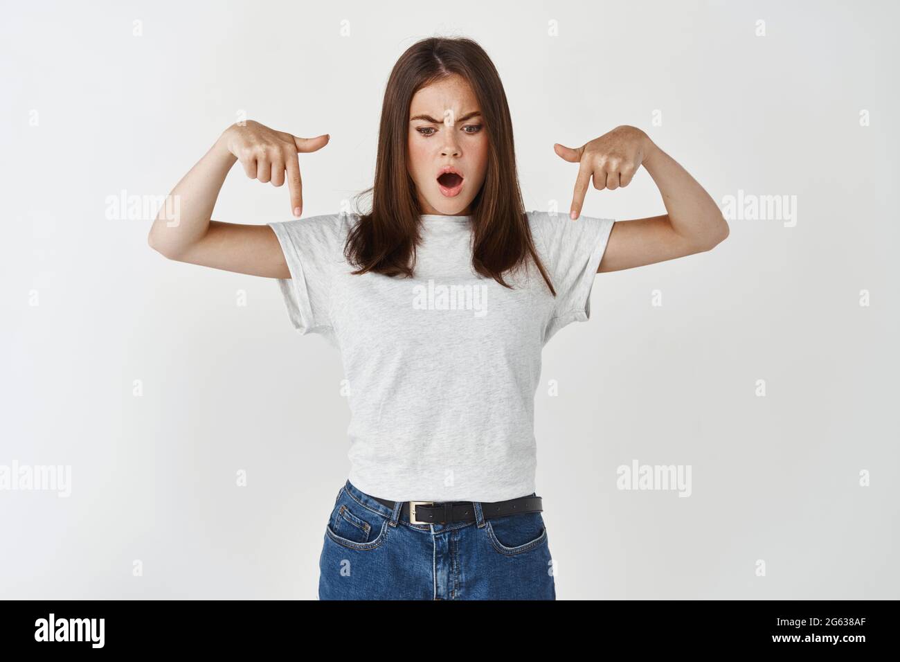 Disappointed and shocked young woman staring, pointing fingers down at ...