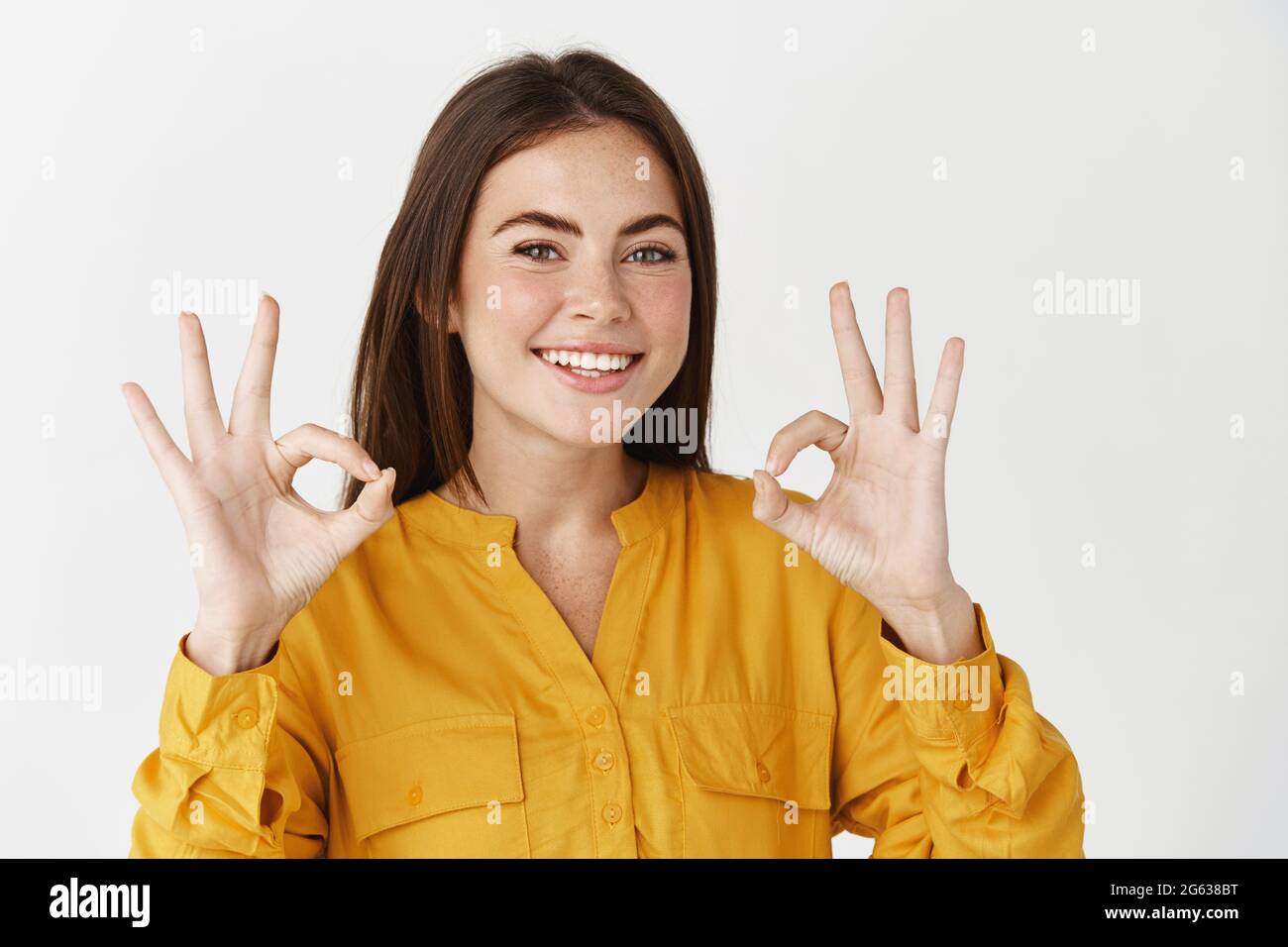 Close-up of smiling young woman assuring you, showing okay sign and ...
