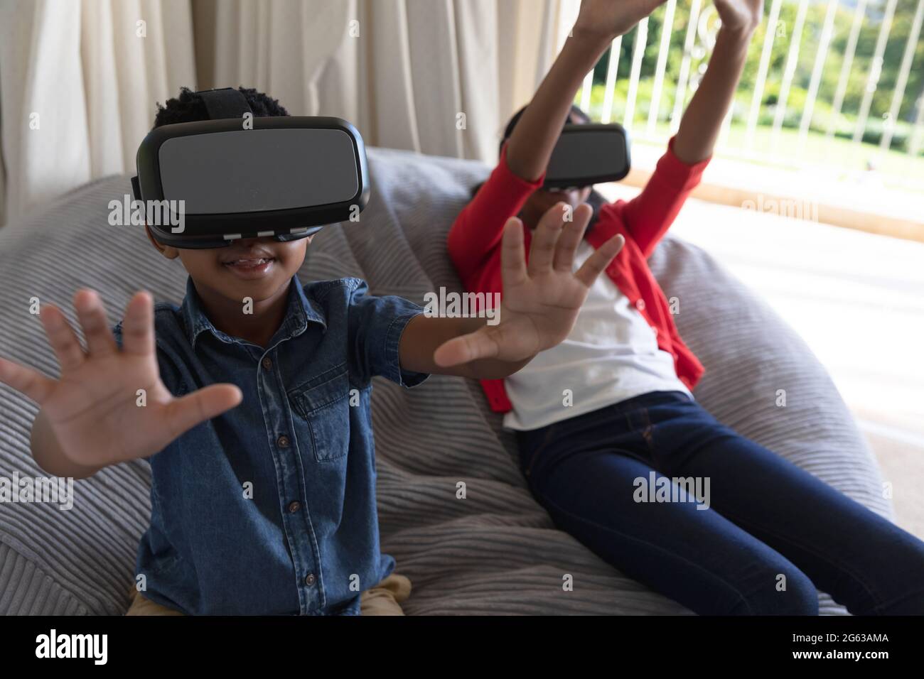 Happy african american boy and girl using vr headsets and smiling at ...