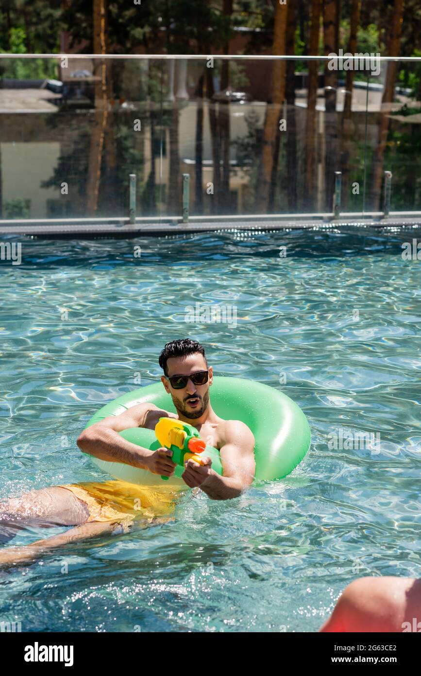 excited muslim man floating on swim ring and playing water gun in pool ...