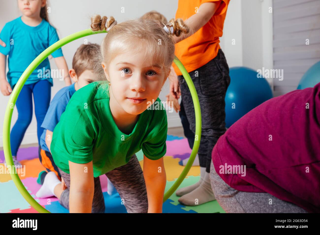 Curly girl crawling on colorful floor through hula hoops Stock Photo ...