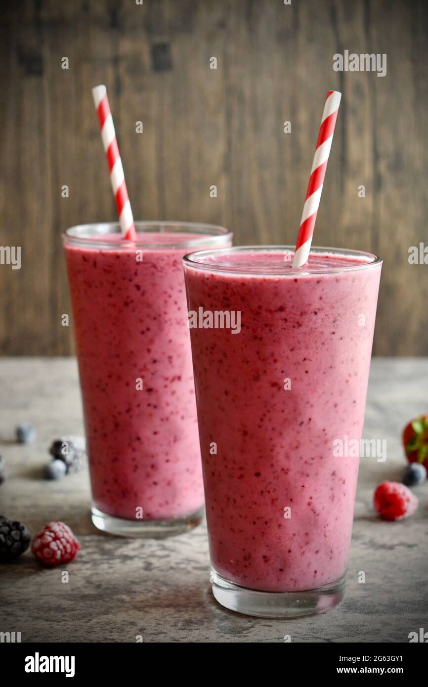 Two mixed berry smoothies in tall decorative glasses on stone surface ...