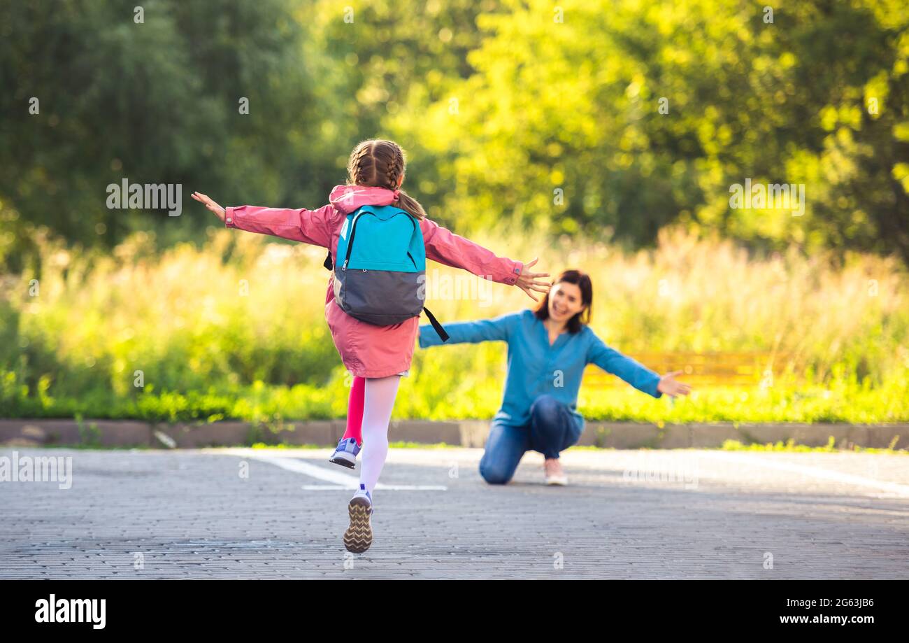 Back view of school girl running to mother after class on sunny street ...