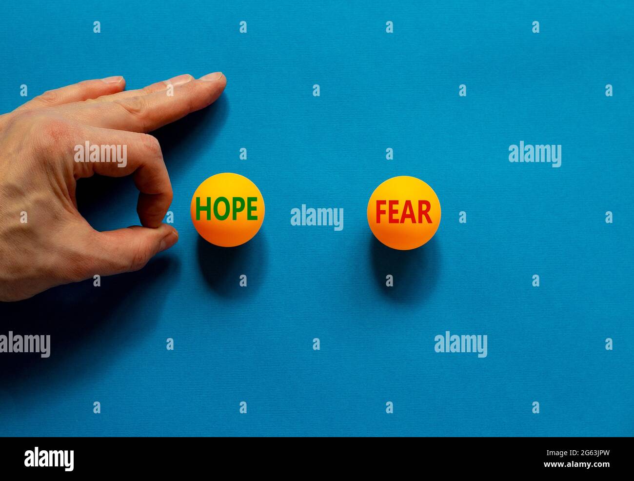 Fear vs hope symbol. Male hand is about to flick the ball. Orange table ...